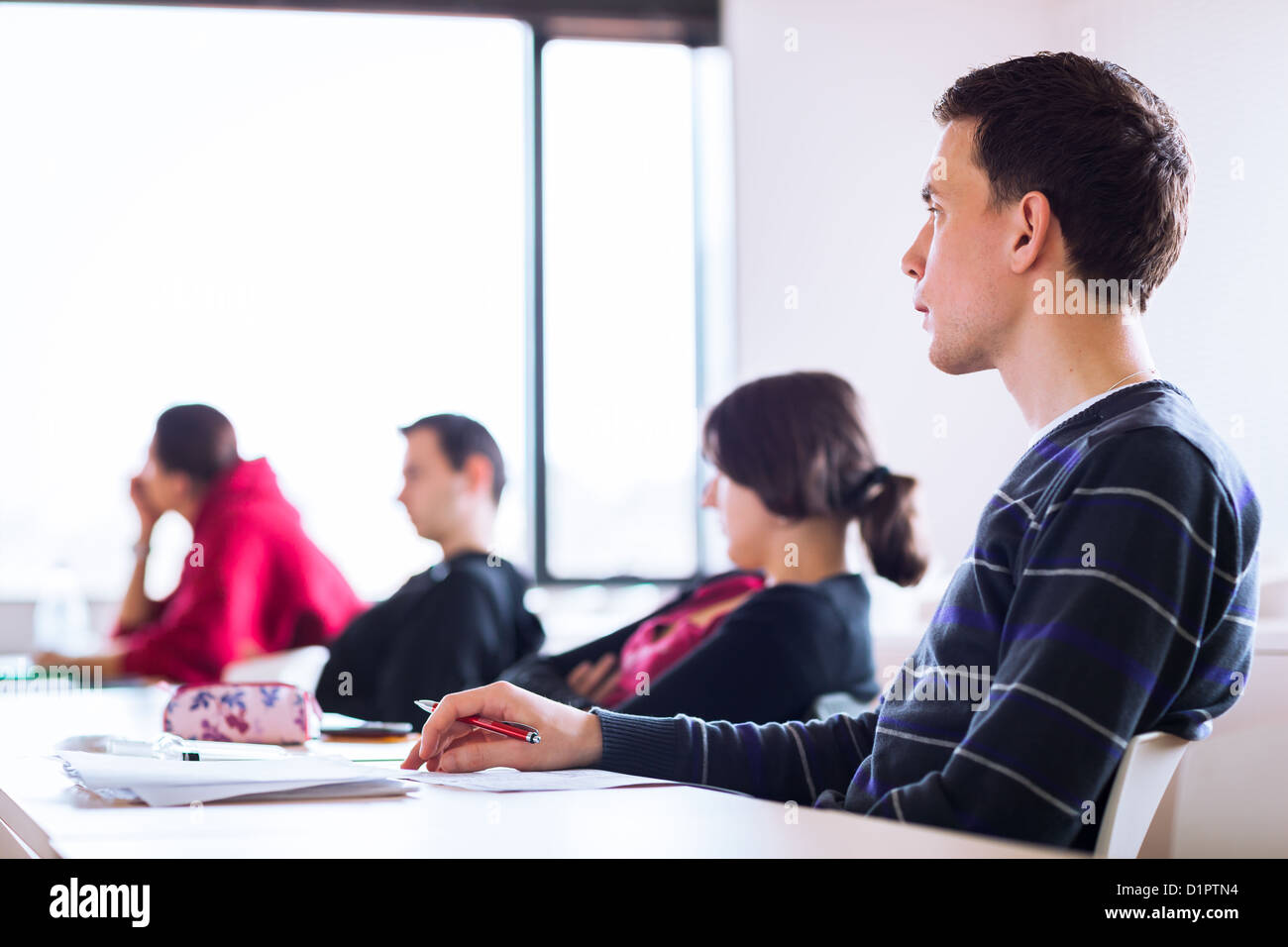 young, handsome male college student sitting in a classroom full of ...