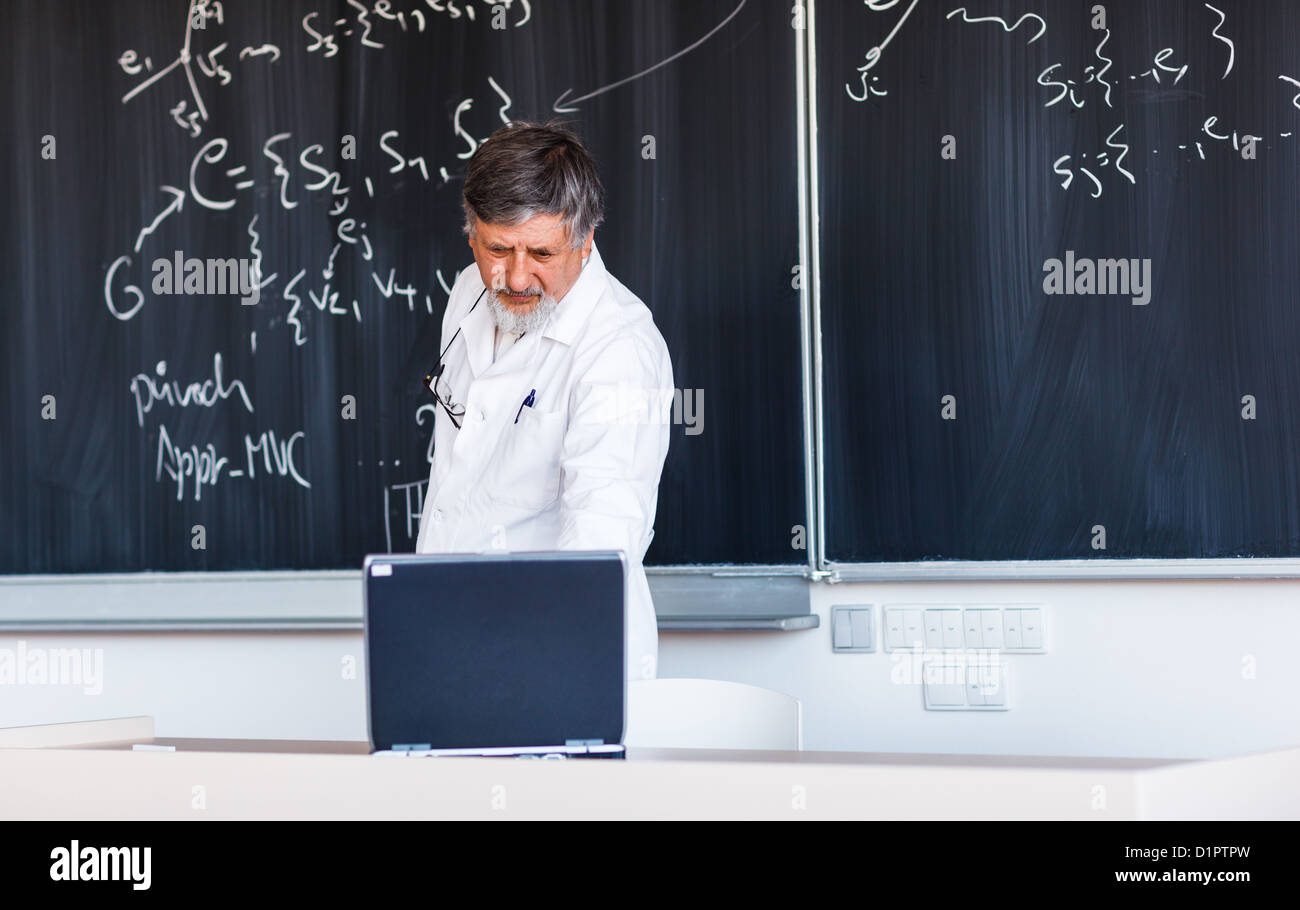 Senior chemistry professor writing on the board while having a chalk ...