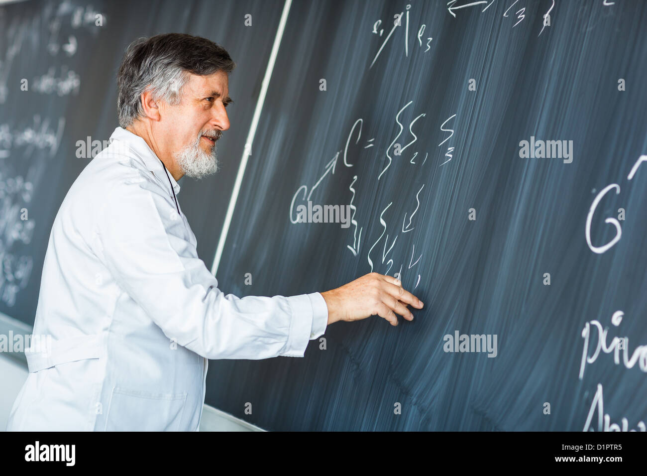 Senior chemistry professor writing on the board while having a chalk ...