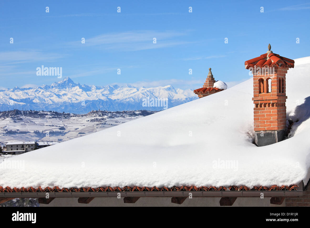 Red brick chimney on the roof covered by snow and snowy mountains on ...