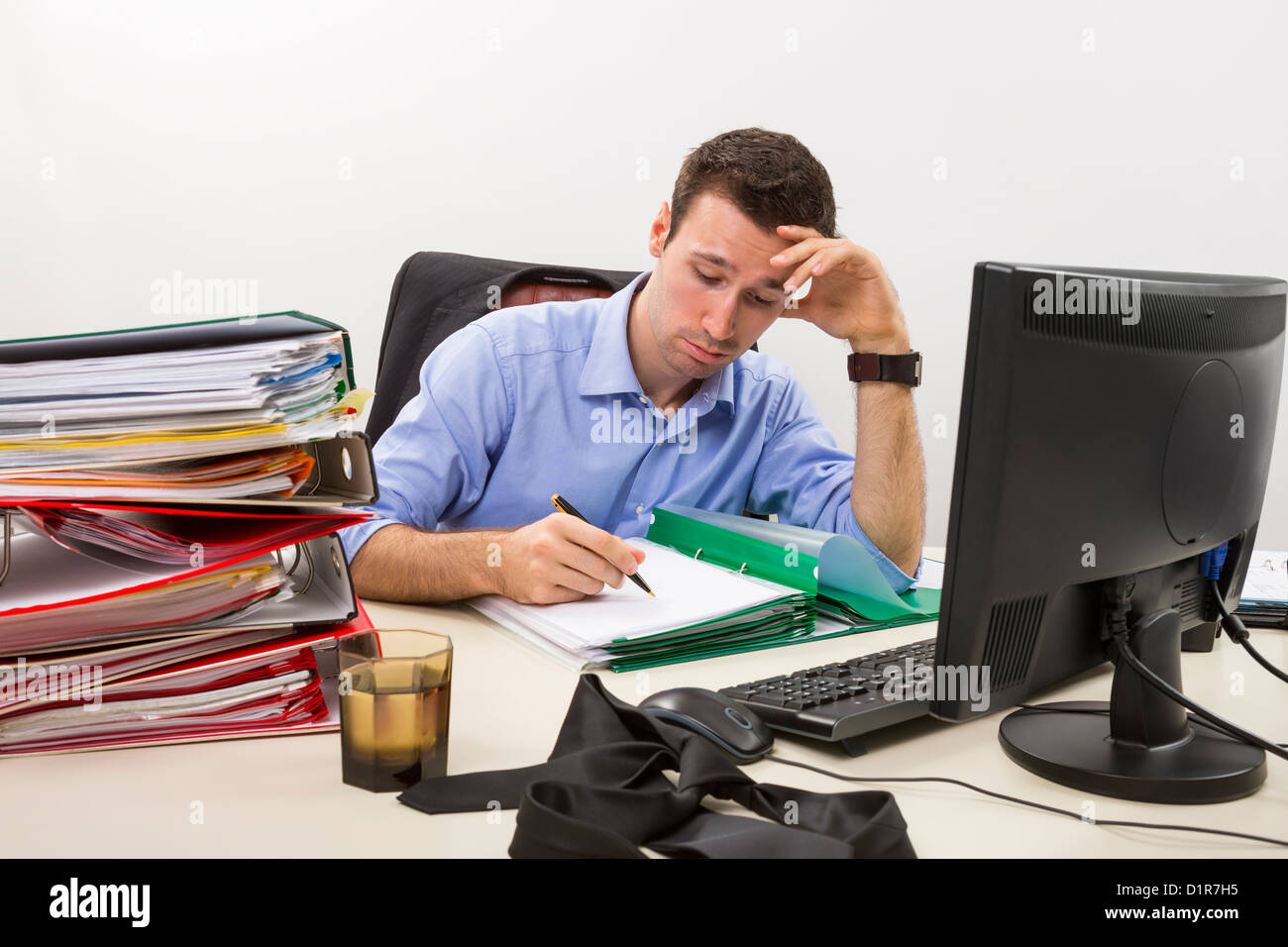Stressed businessman filling paper documents in front of his computer ...