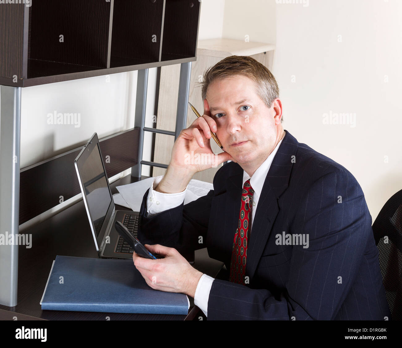 Mature man holding calculator while thinking with computer and papers ...