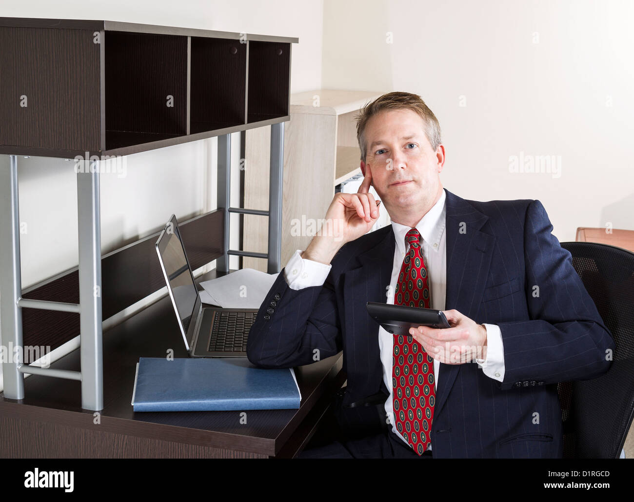 Mature man holding calculator while leaning back in chair with computer ...