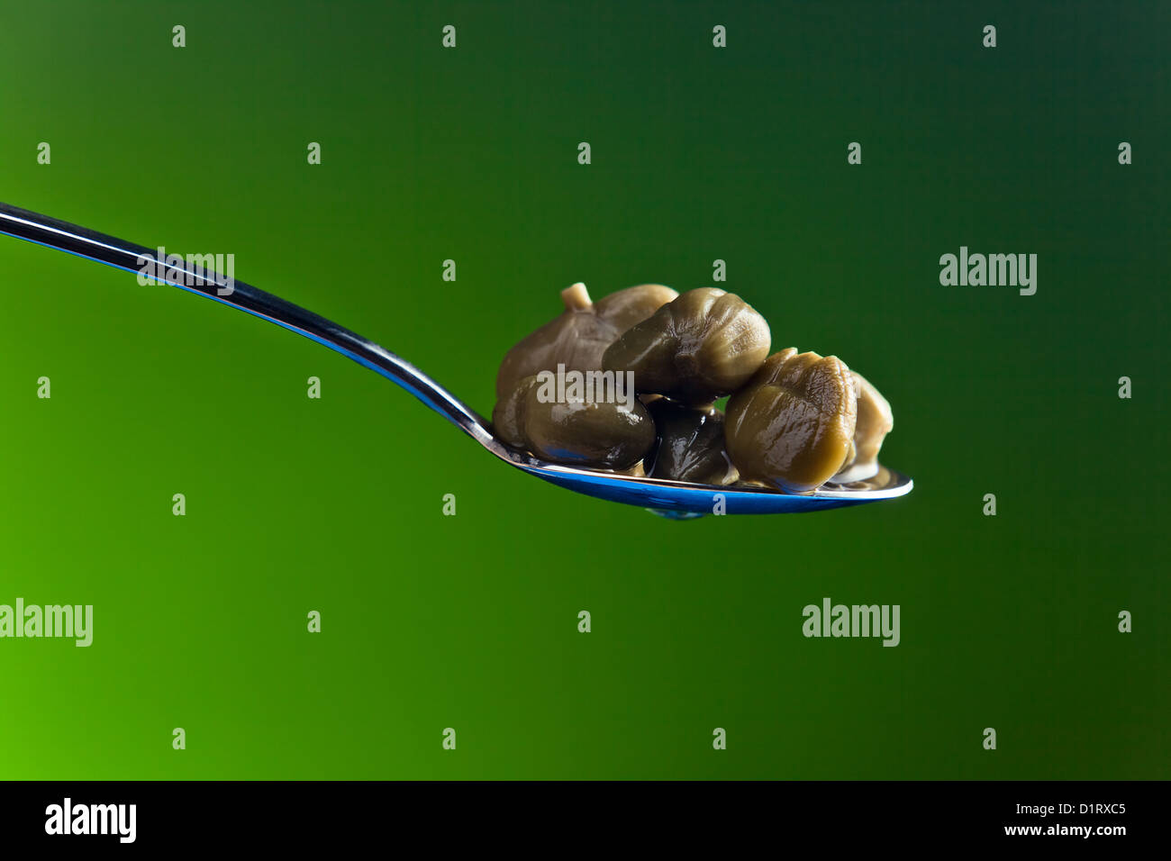 Marinated capers in spoon on a green background Stock Photo - Alamy
