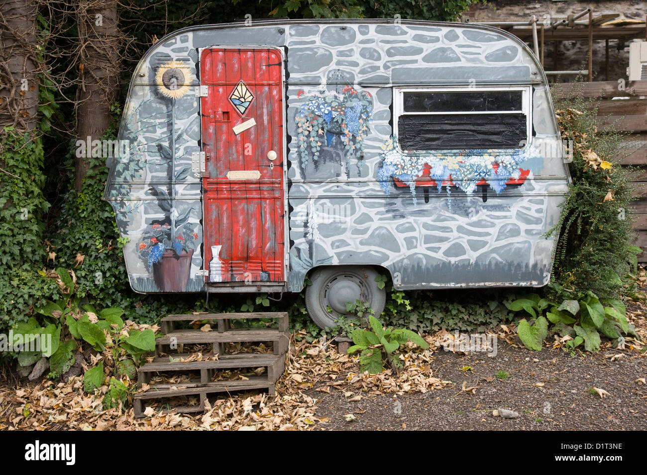 A small caravan decorated as a house with front door and painted stone ...