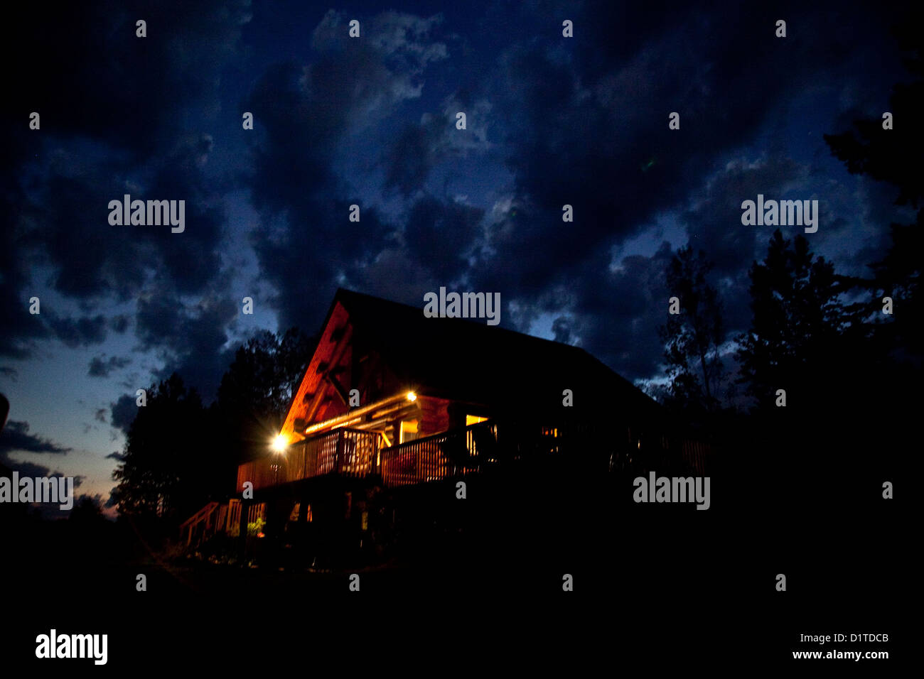 A warmly lit cottage home is set against a dark blue clouded sunsetting ...