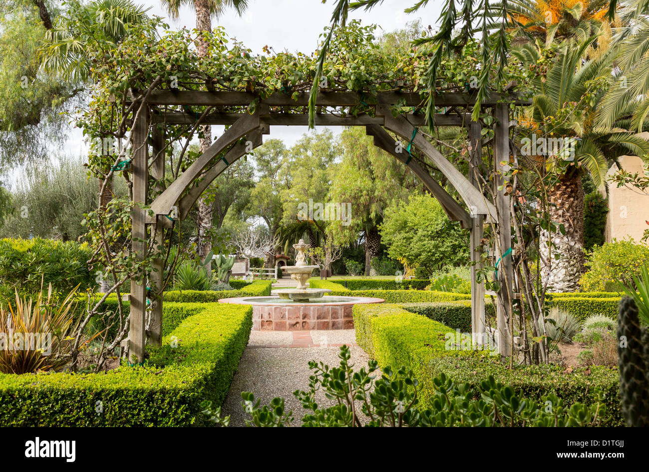 Traditional landscaped garden with rose trellis and fountain with ...