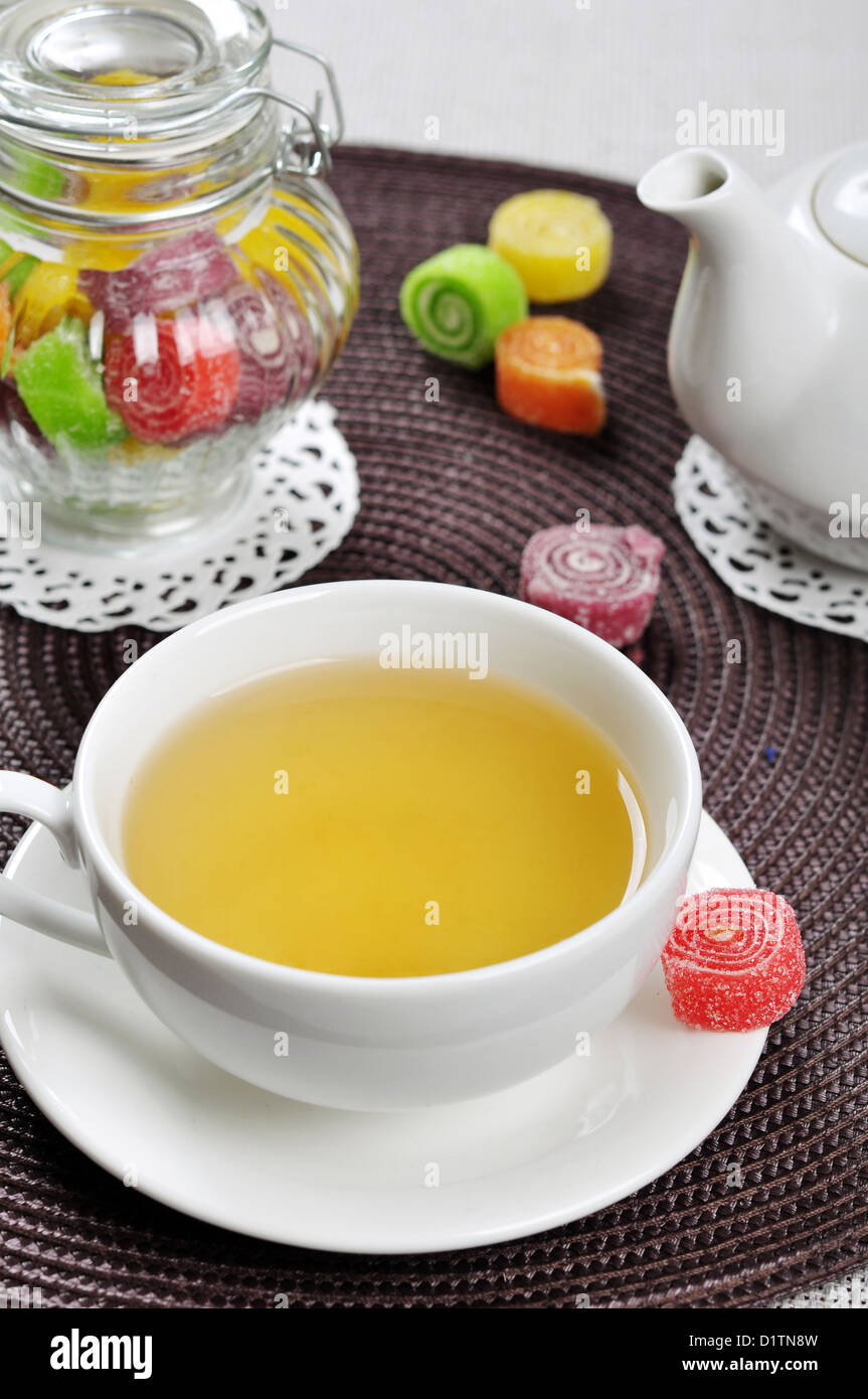 Tea in cup, sweet jelly candies in glass jar and teapot Stock Photo - Alamy