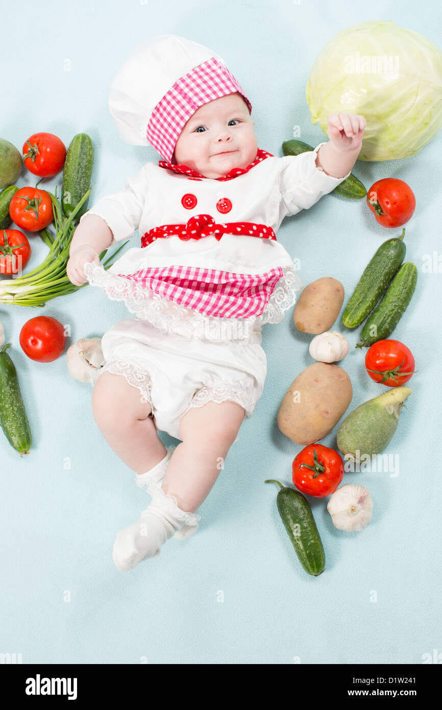 Portrait of smiling baby wearing a chef hat surrounded by vegetables ...