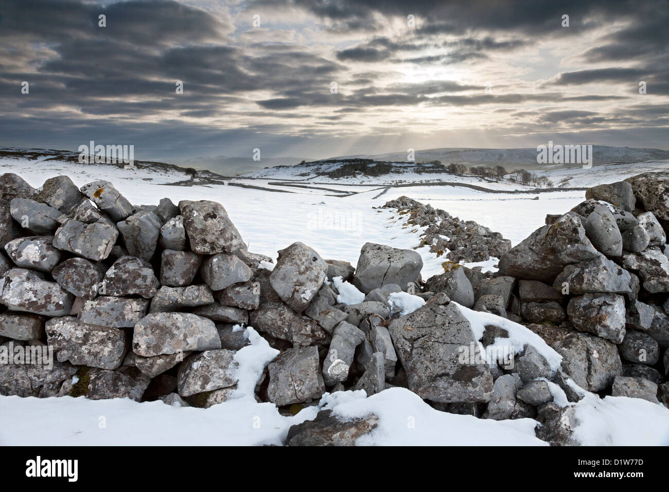 A crumbling dry stone wall pictured in snow against a dramatic sky near ...