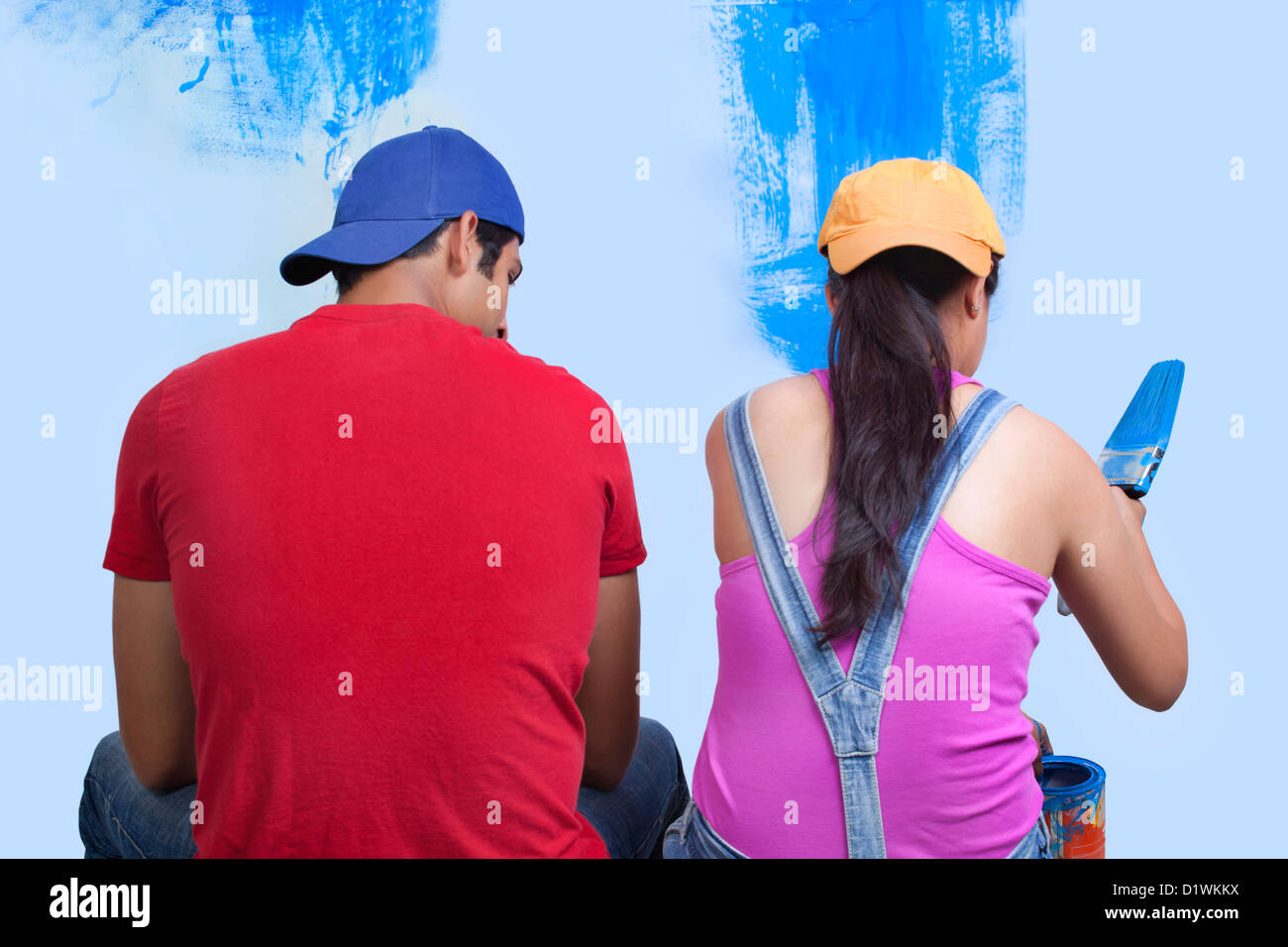 Rear view of young couple sitting with incomplete painted wall Stock ...