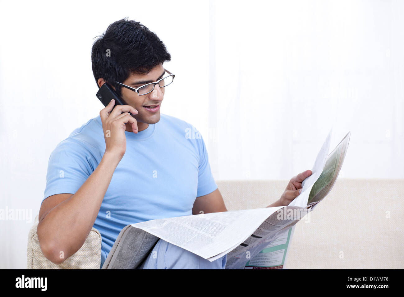 Young man reading newspaper while talking on mobile phone Stock Photo ...