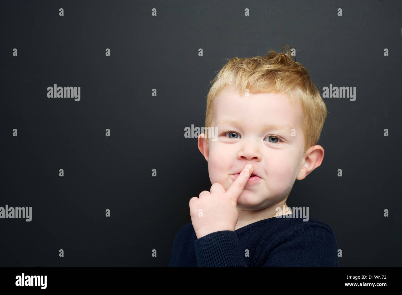 Smart young boy wearing a navy blue jumper with his finger over his ...