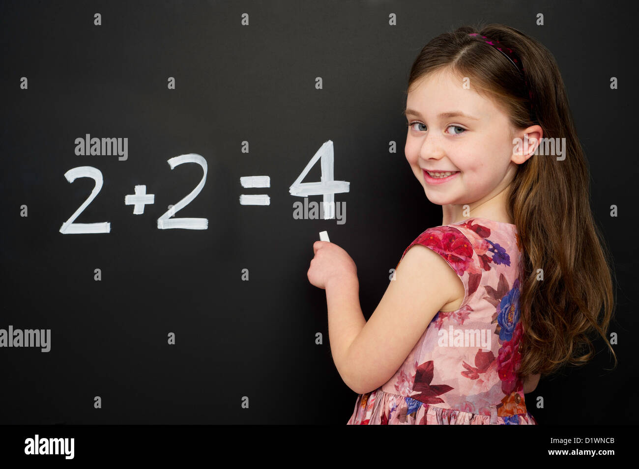 Smart young girl wearing a red dress writing math sums on a blackboard ...