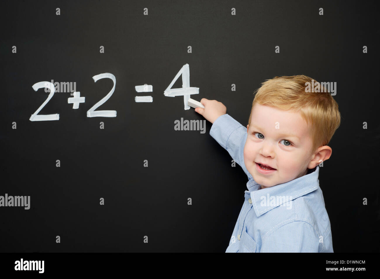 Smart young boy wearing a blue striped shirt stood writing a math sum ...