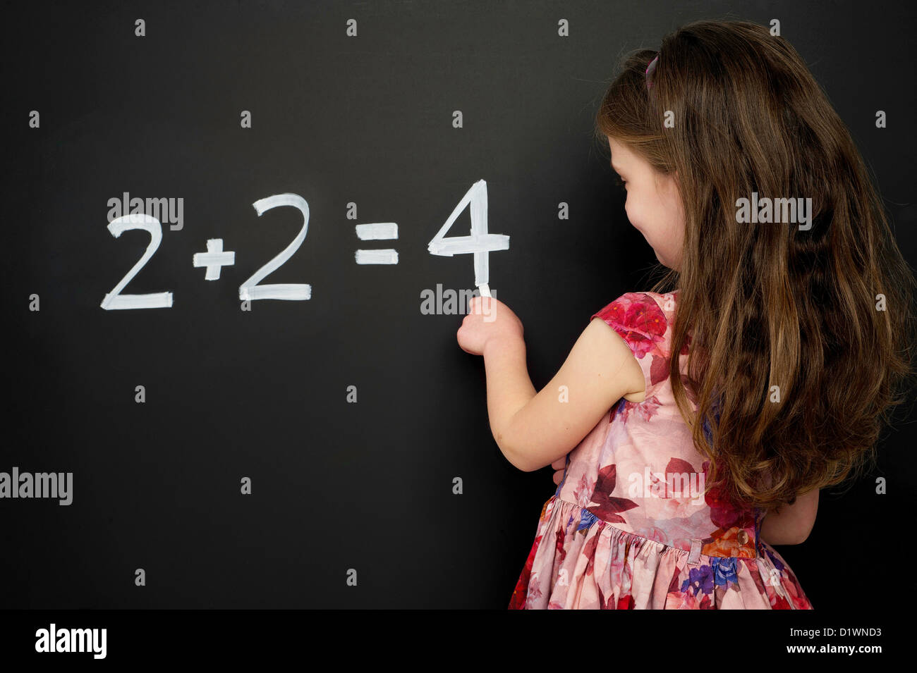 Smart young girl wearing a red dress writing a maths sum on a ...
