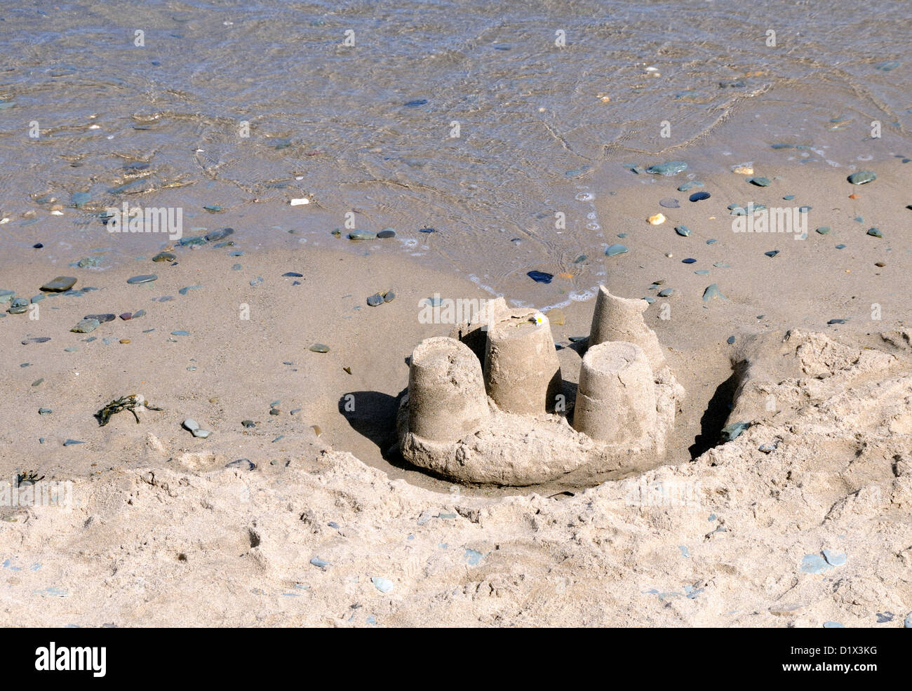 A child's sandcastle on the beach is about to be washed away by the ...