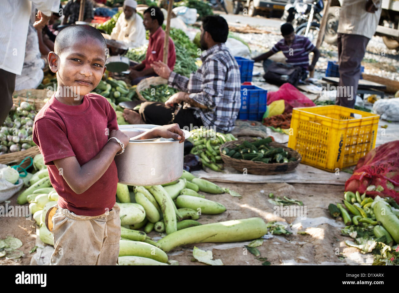 Poor young Indian street boy carrying pots in front of a street market ...