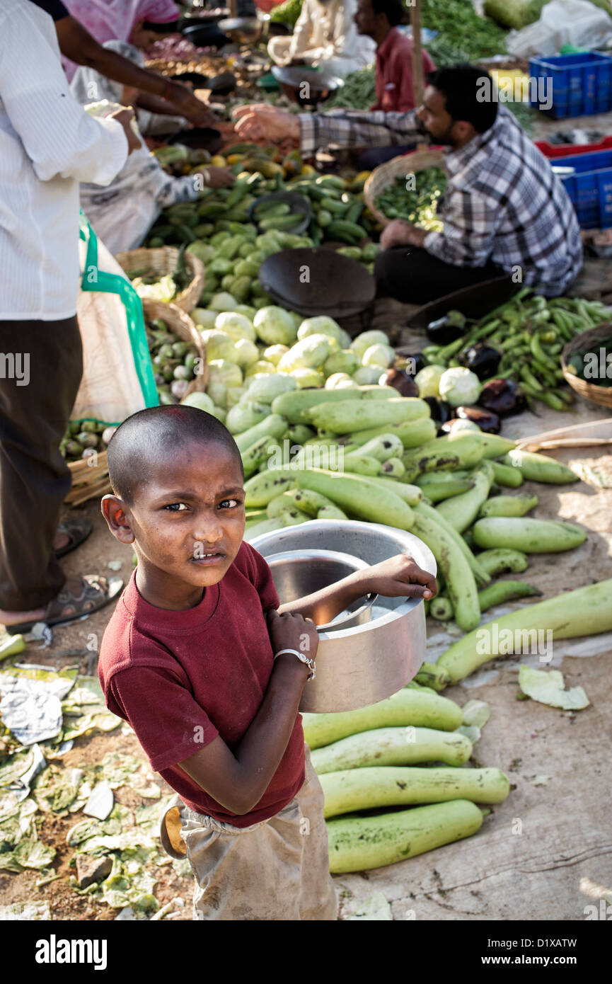 Poor young Indian street boy carrying pots in front of a street market ...