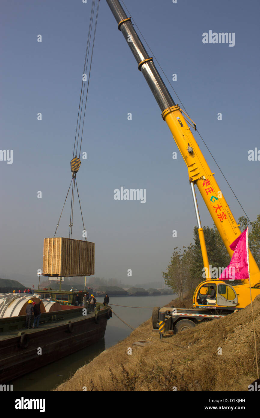 Crane lifting large wooden box off a barge at Huinanzhuang pumping ...
