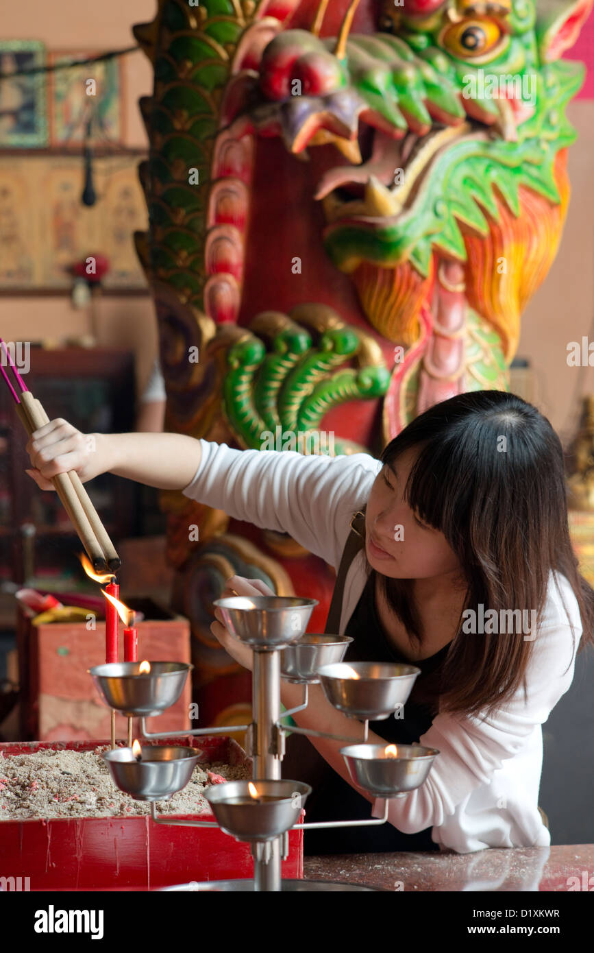 A young Buddhist devotee lights incense as offerings in the Guan Di ...