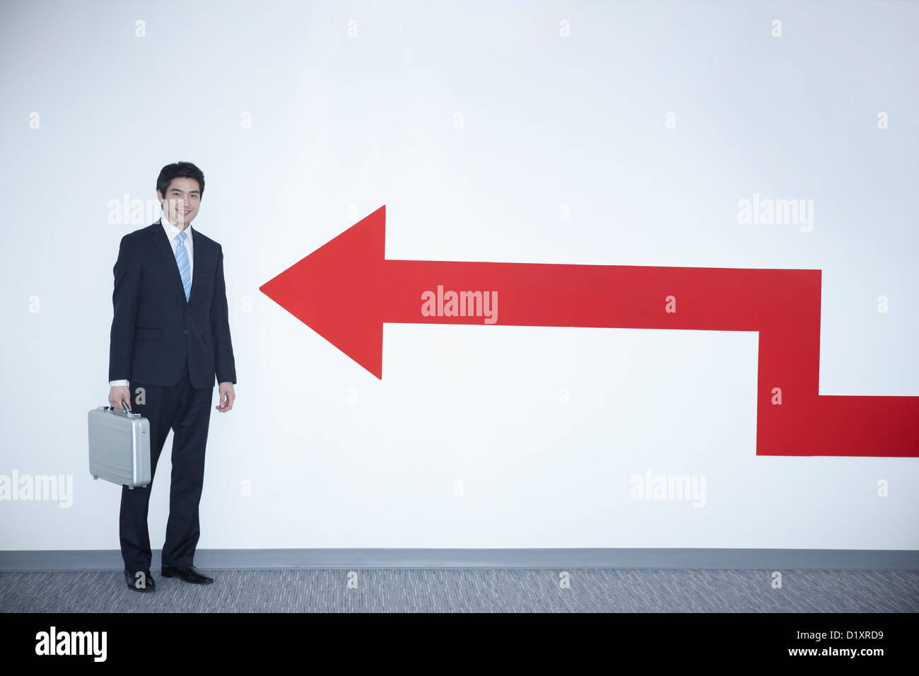 a businessman standing to an arrow on the wall Stock Photo - Alamy