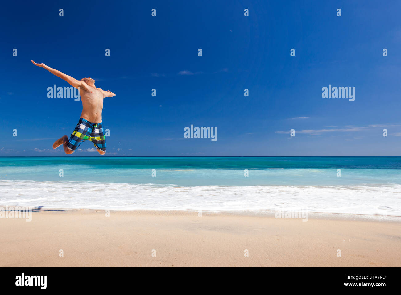 Athletic young man enjoying the summer, jumping in a tropical beach ...