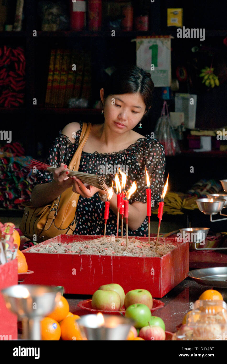 A young Buddhist devotee lights incense as offerings in the Guan Di ...