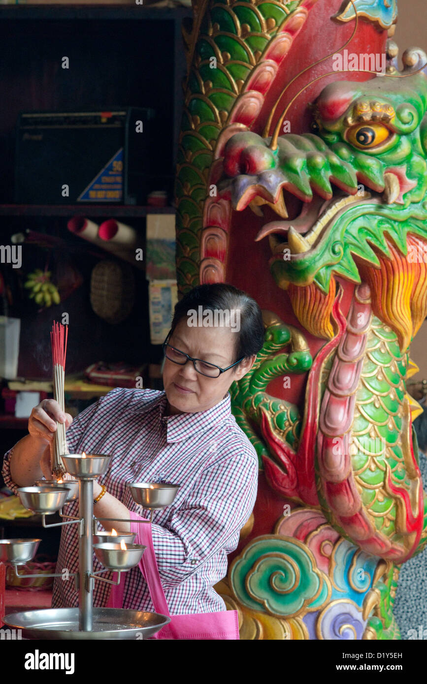 A Buddhist devotee lights incense as offerings in the Guan Di Chinese ...