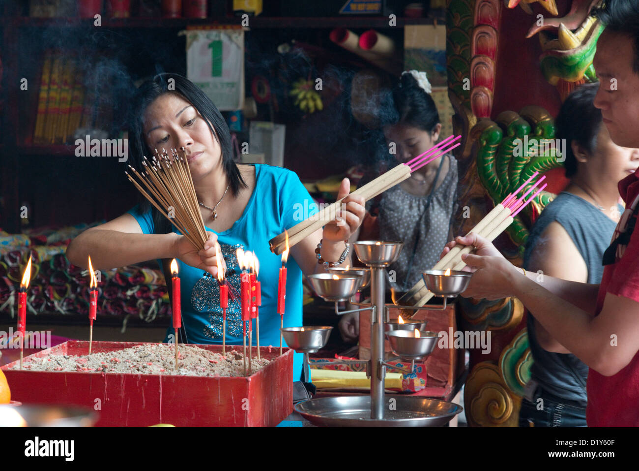 A Buddhist devotee lights incense as offerings in the Guan Di Chinese ...