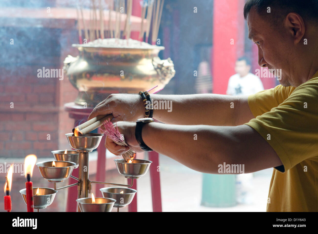 A Buddhist devotee lights incense as offerings in the Guan Di Chinese ...