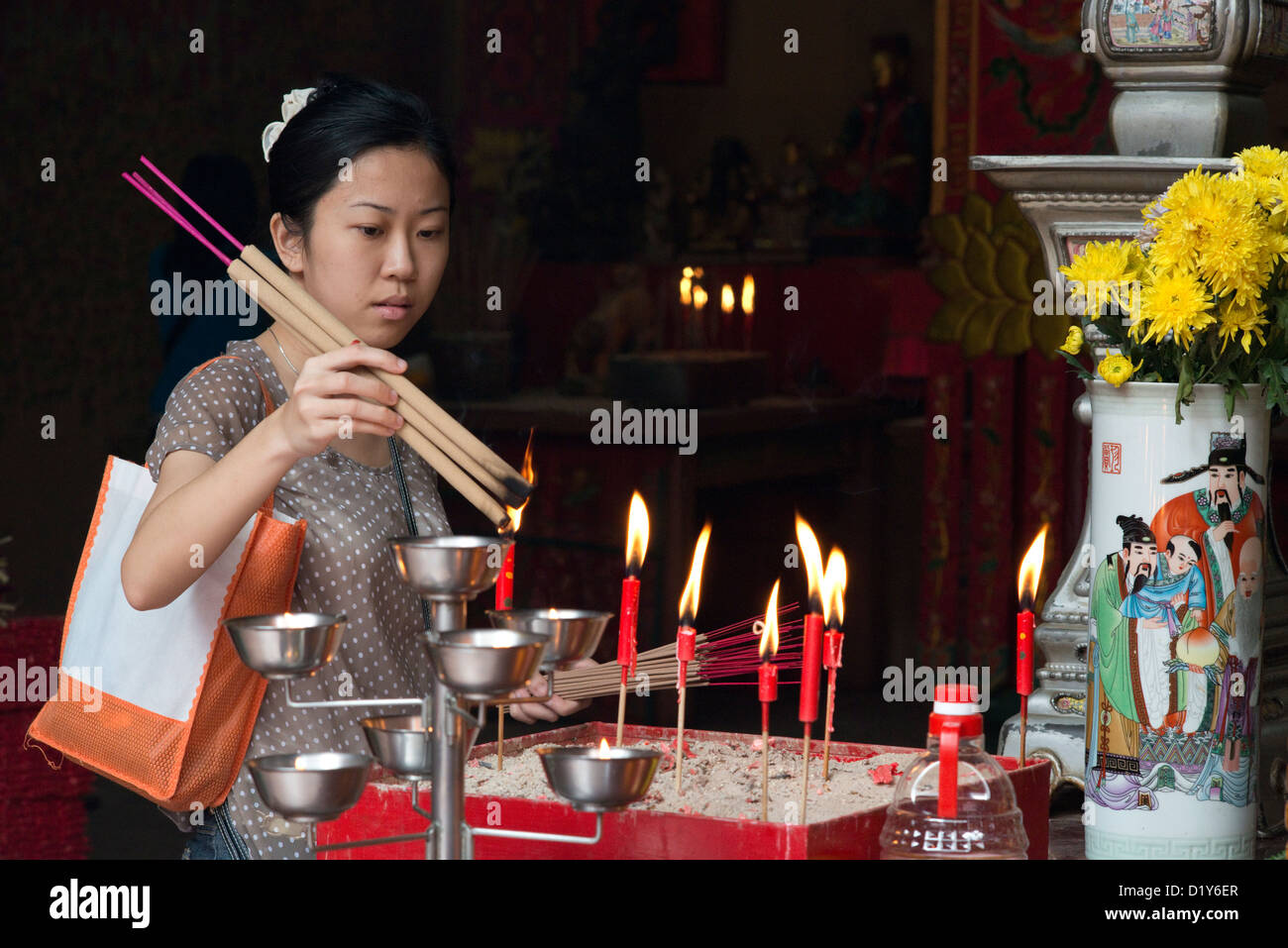 A young Buddhist devotee lights incense as offerings in the Guan Di ...