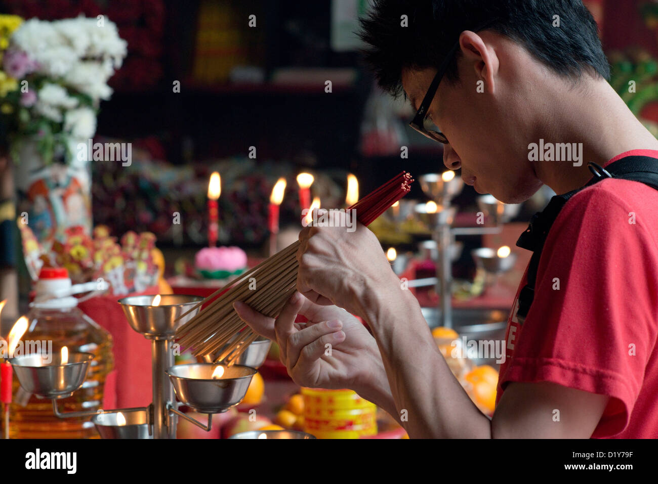A young Buddhist devotee lights incense as offerings in the Guan Di ...