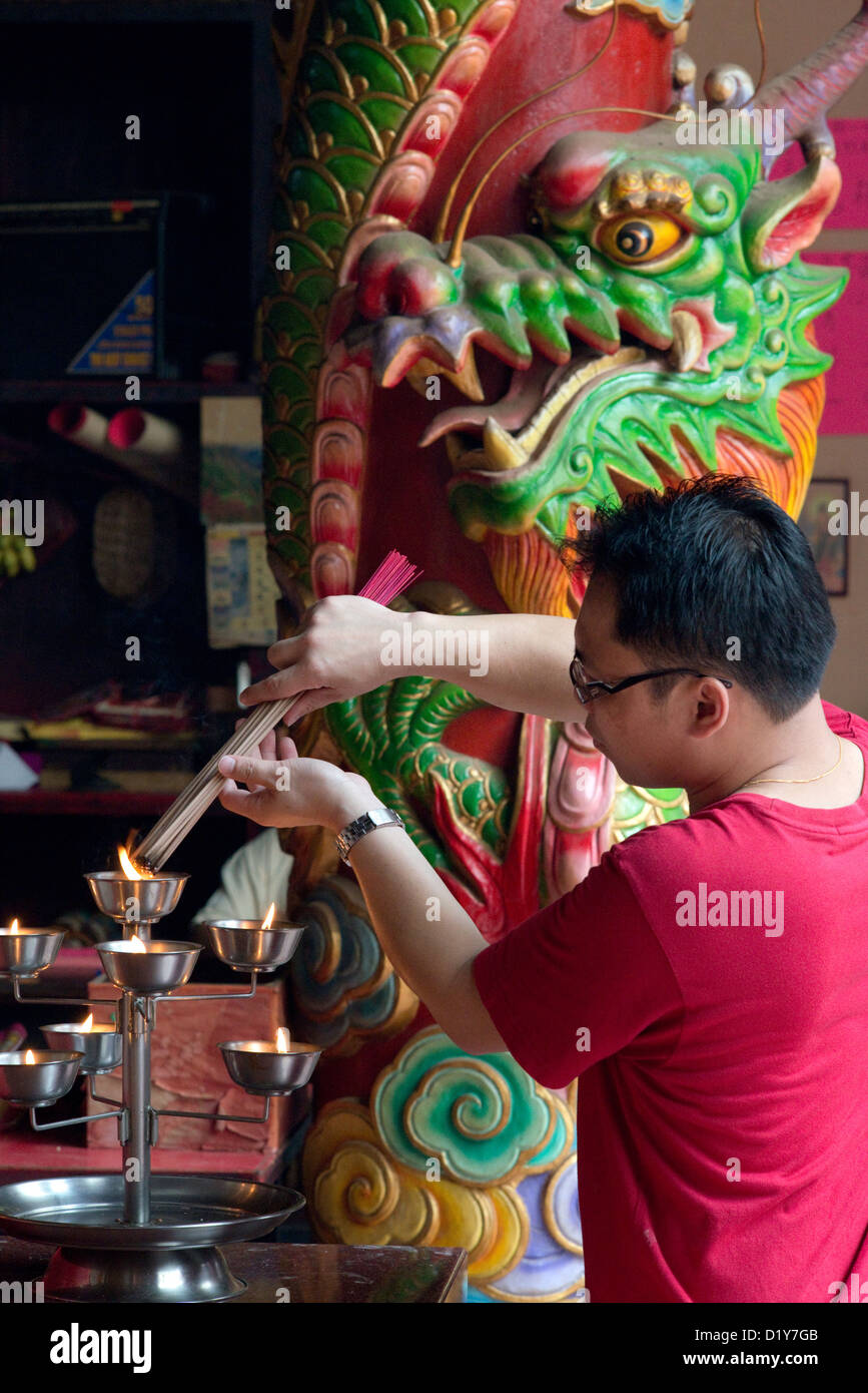 A Buddhist devotee lights incense as offerings in the Guan Di Chinese ...