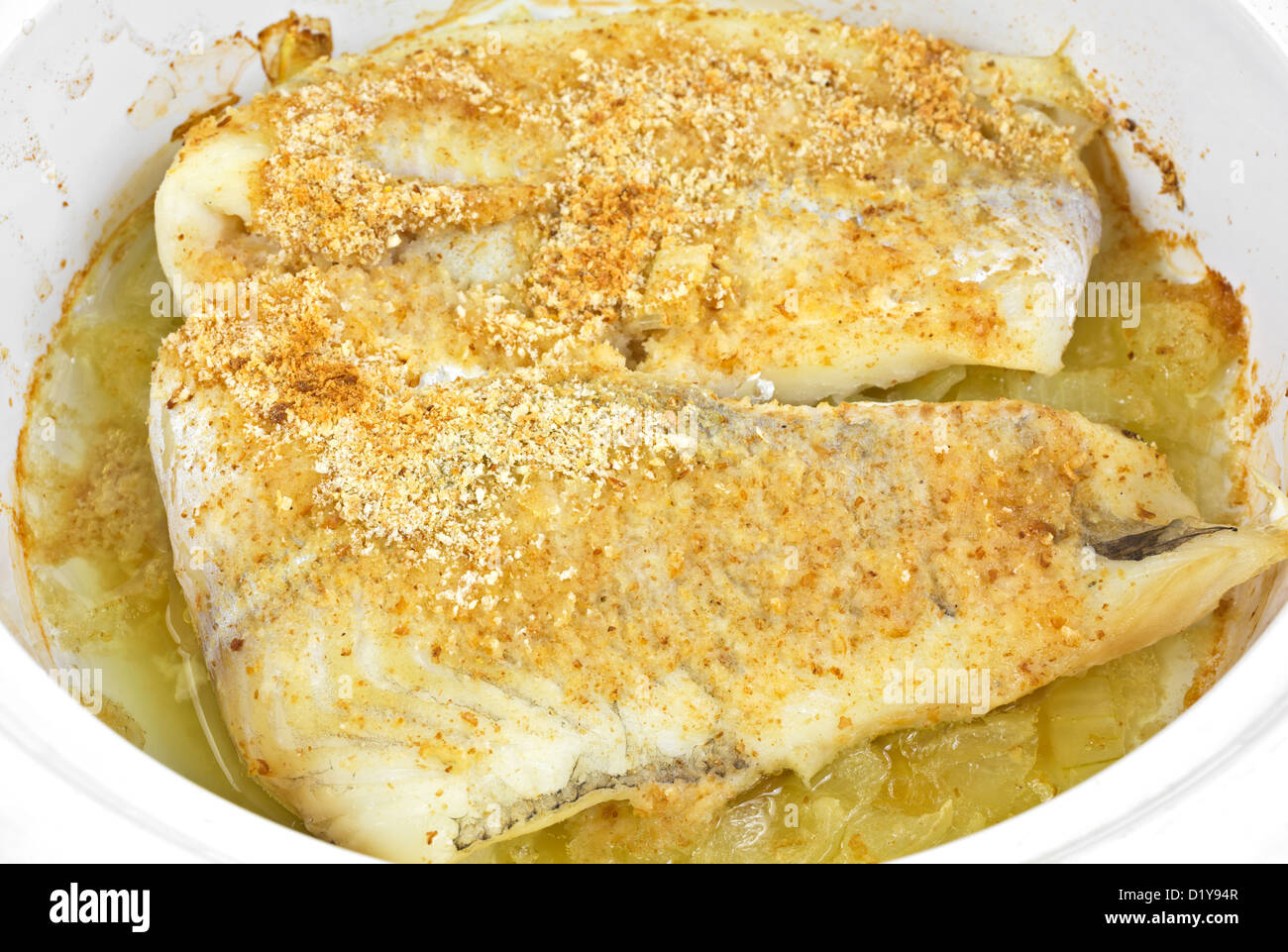A close view of cooked breaded haddock atop onions in a baking dish ...