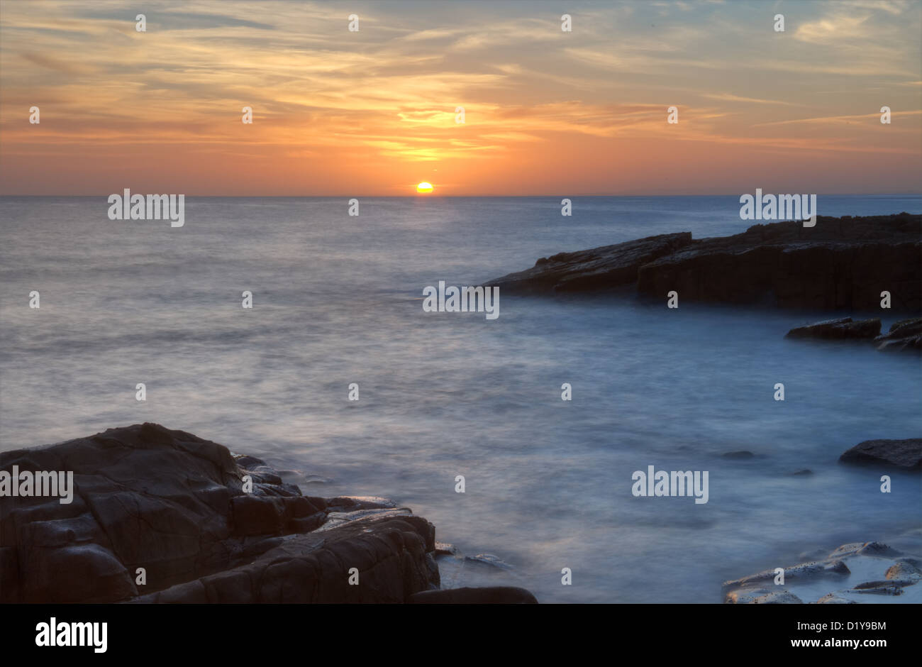 a sunset over a beach with rocks Stock Photo - Alamy