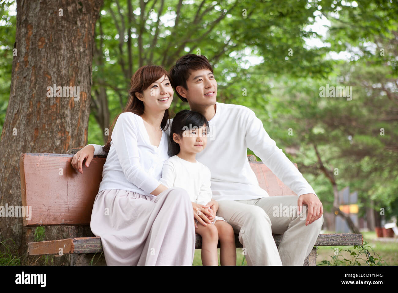 parents with a female kid sitting on a bench Stock Photo - Alamy
