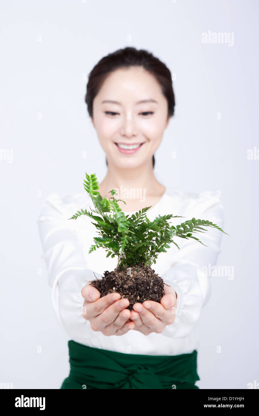 a woman in green skirt giving a plant with roots Stock Photo - Alamy