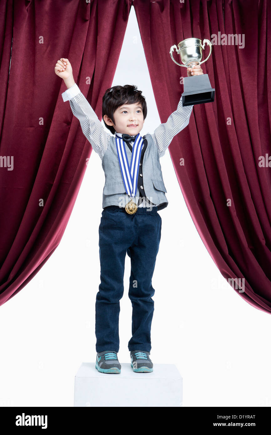 a kid raising hands with a trophy cup in front of a red curtains Stock ...