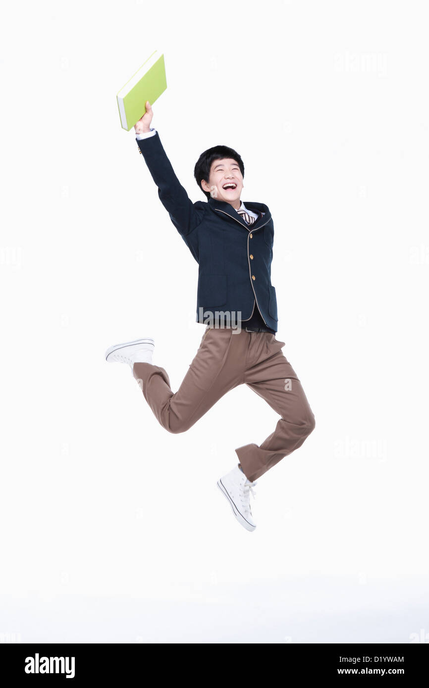 a male student wearing school uniform jumping while holding a book ...