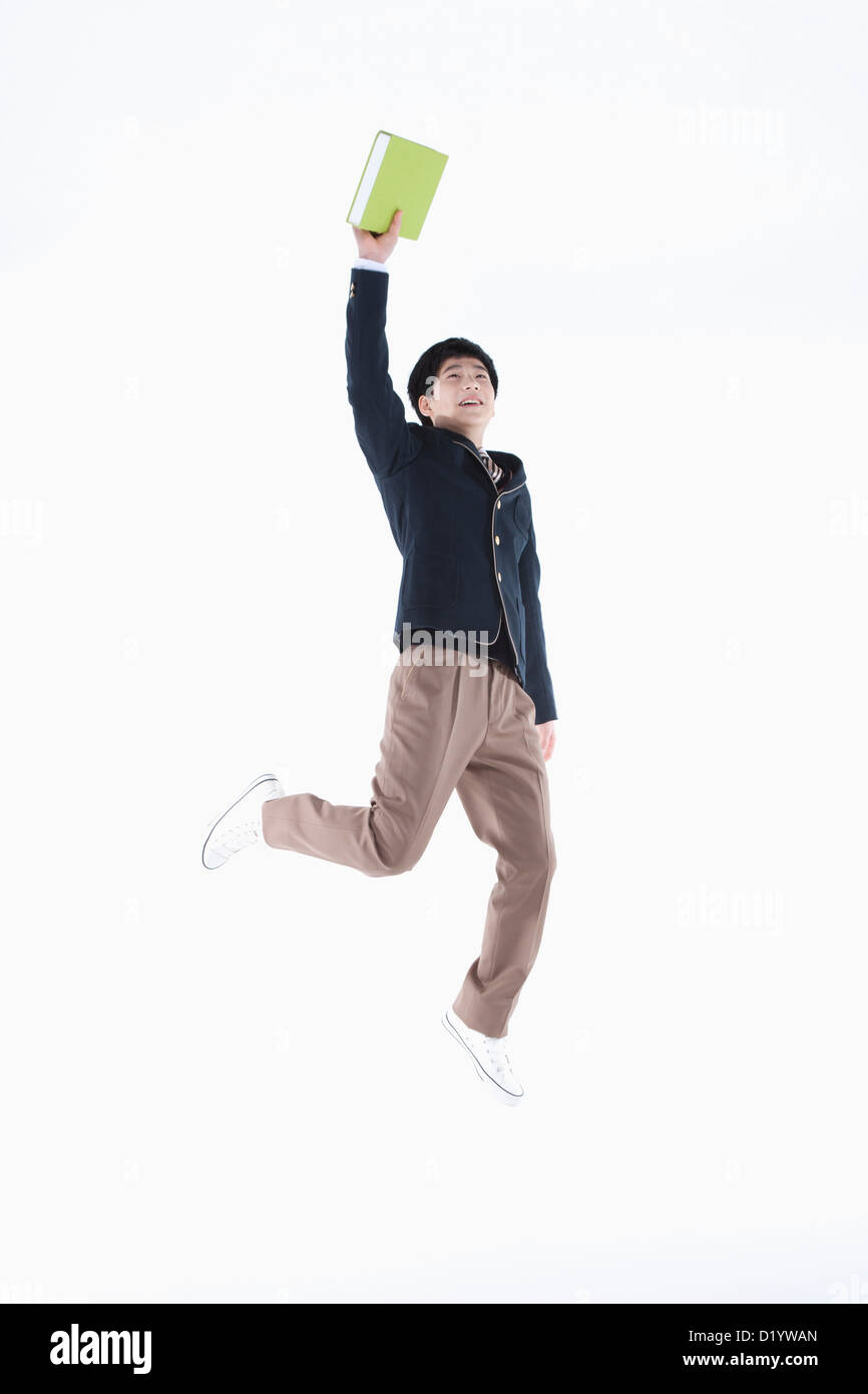 a male student wearing school uniform jumping while holding a book ...