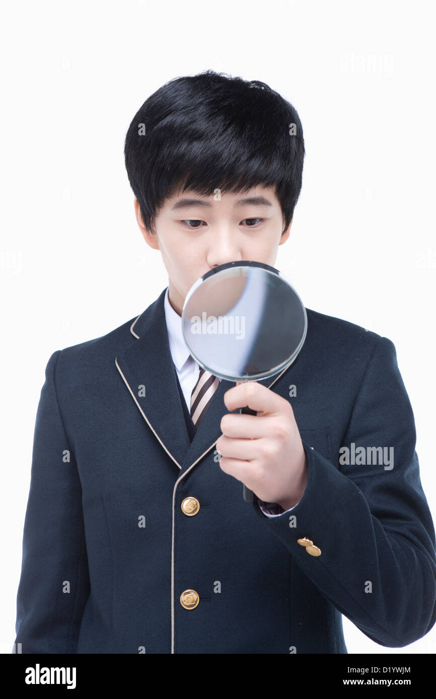 a male student with school uniform looking through a magnifying glass ...