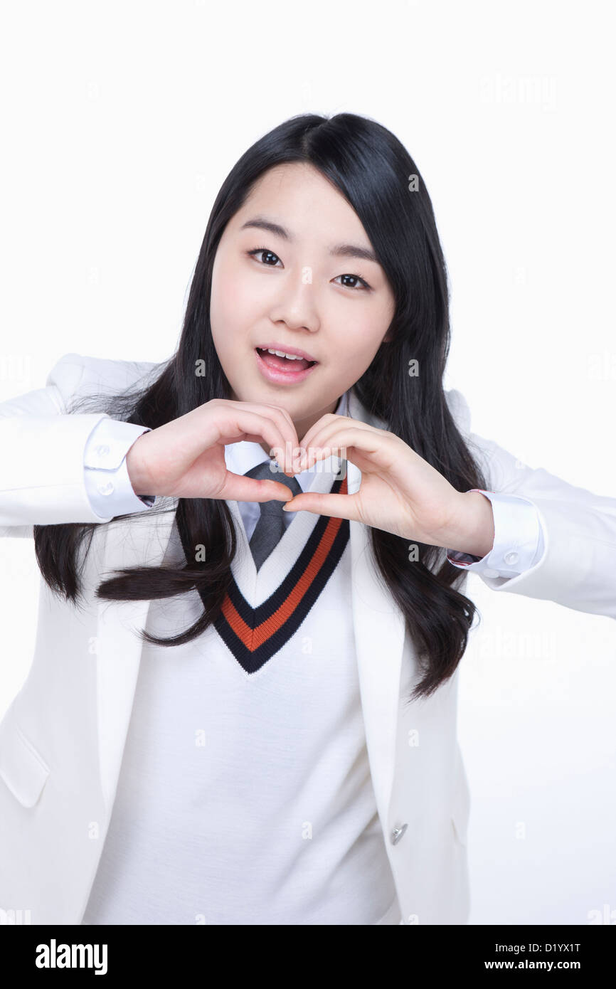 a female student in school uniform making heart symbol with her hands ...