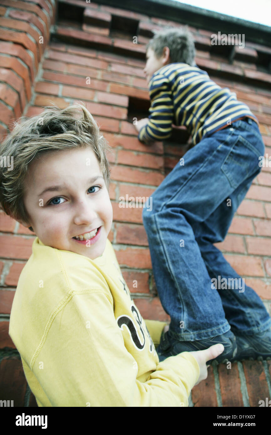 Boy giving friend a bunk-up over a wall Stock Photo - Alamy
