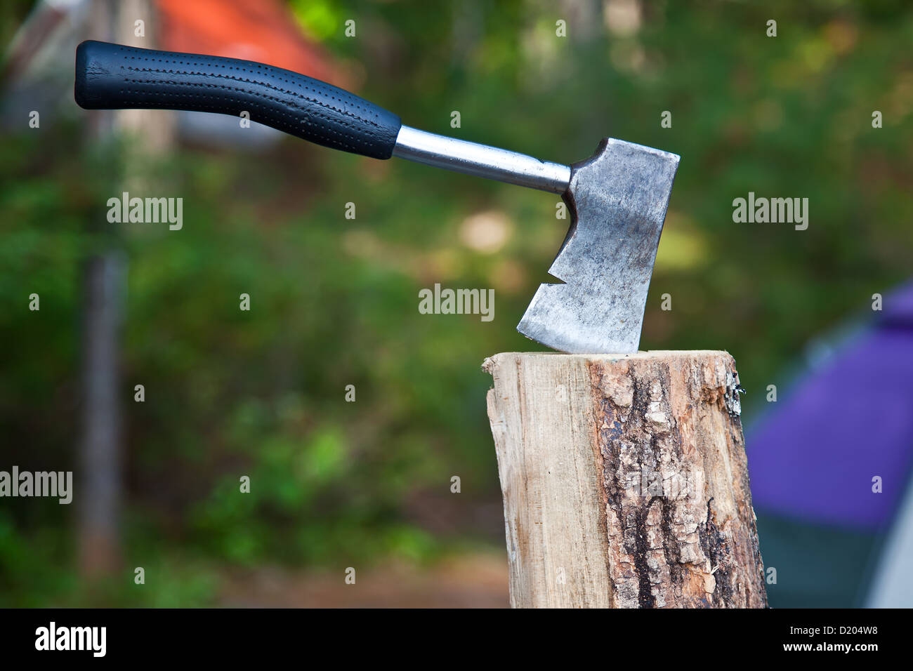 An old, well used hatchet embedding in a block of wood at a camp site ...