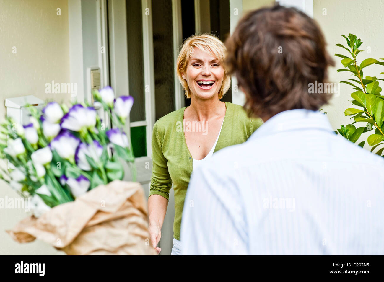 Young women receiving flowers from a young man in front of a house ...