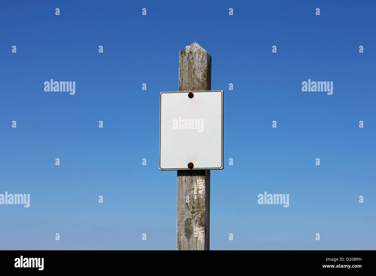 A white, empty sign on a weathered wooden signpost before a clear blue ...