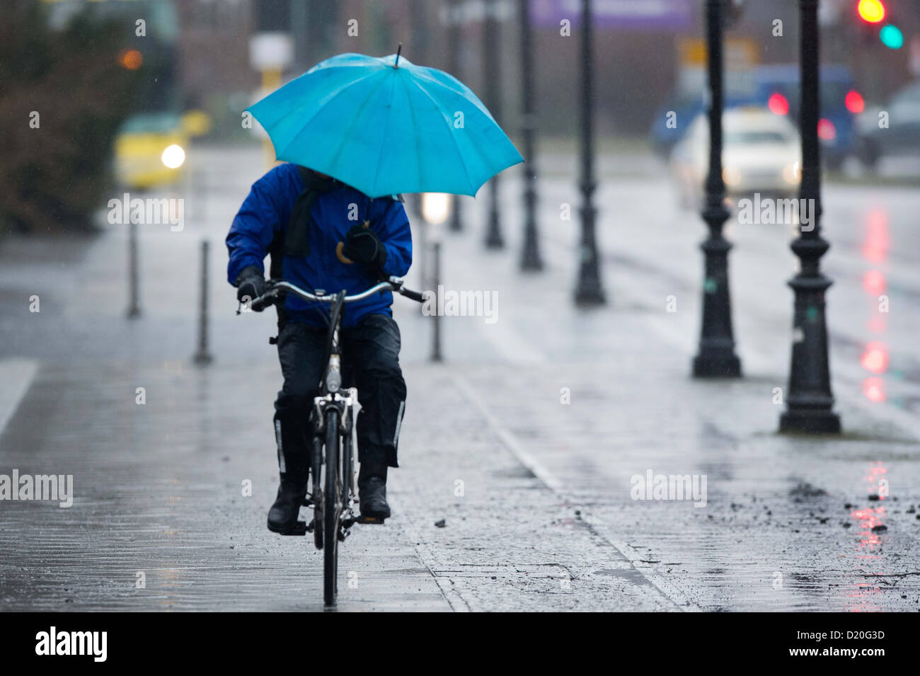 A cyclist tries to protect himself from the rain with an umbrella in ...