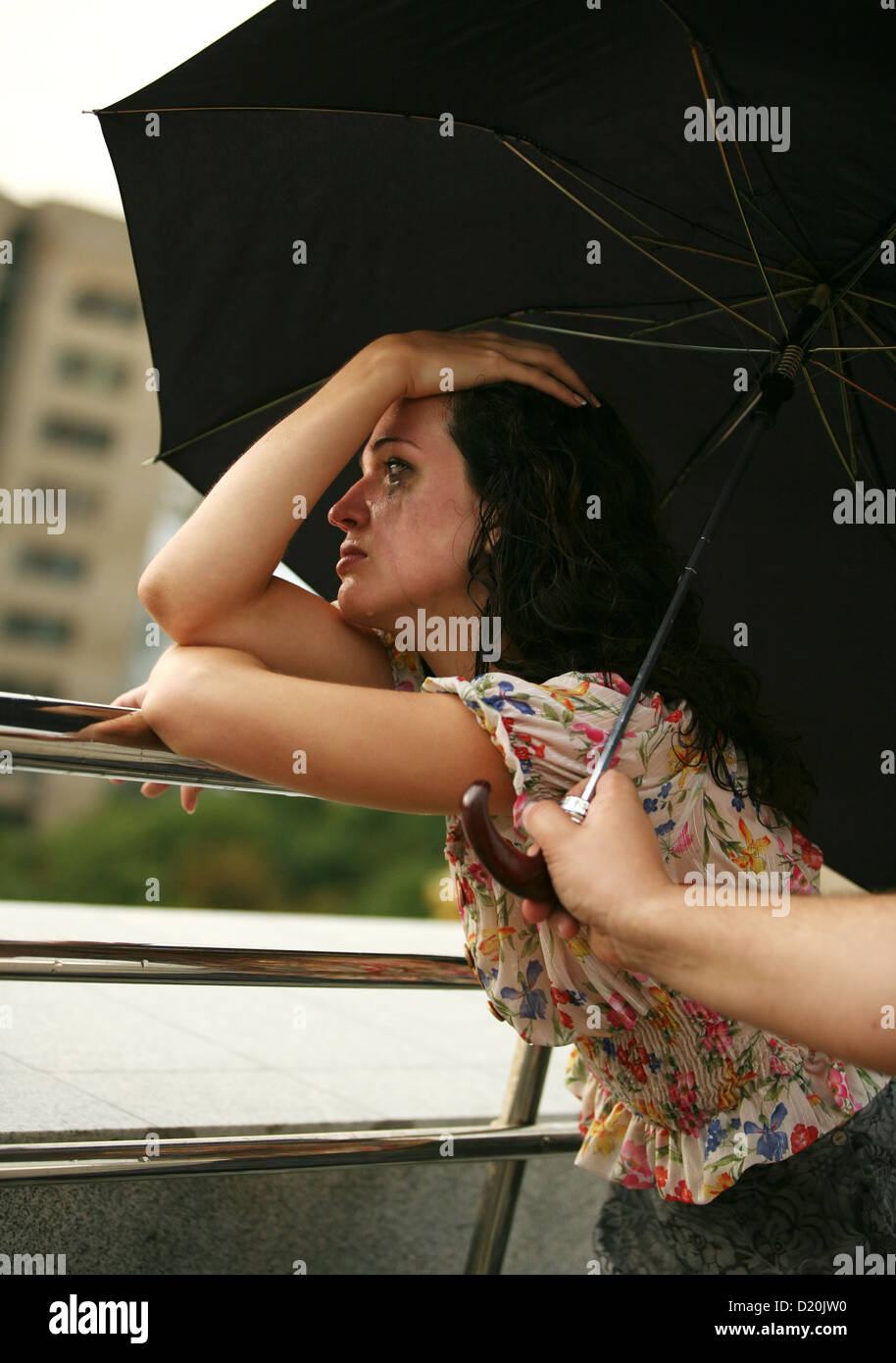 The lonely crying girl. The man covers from a rain a umbrella Stock ...