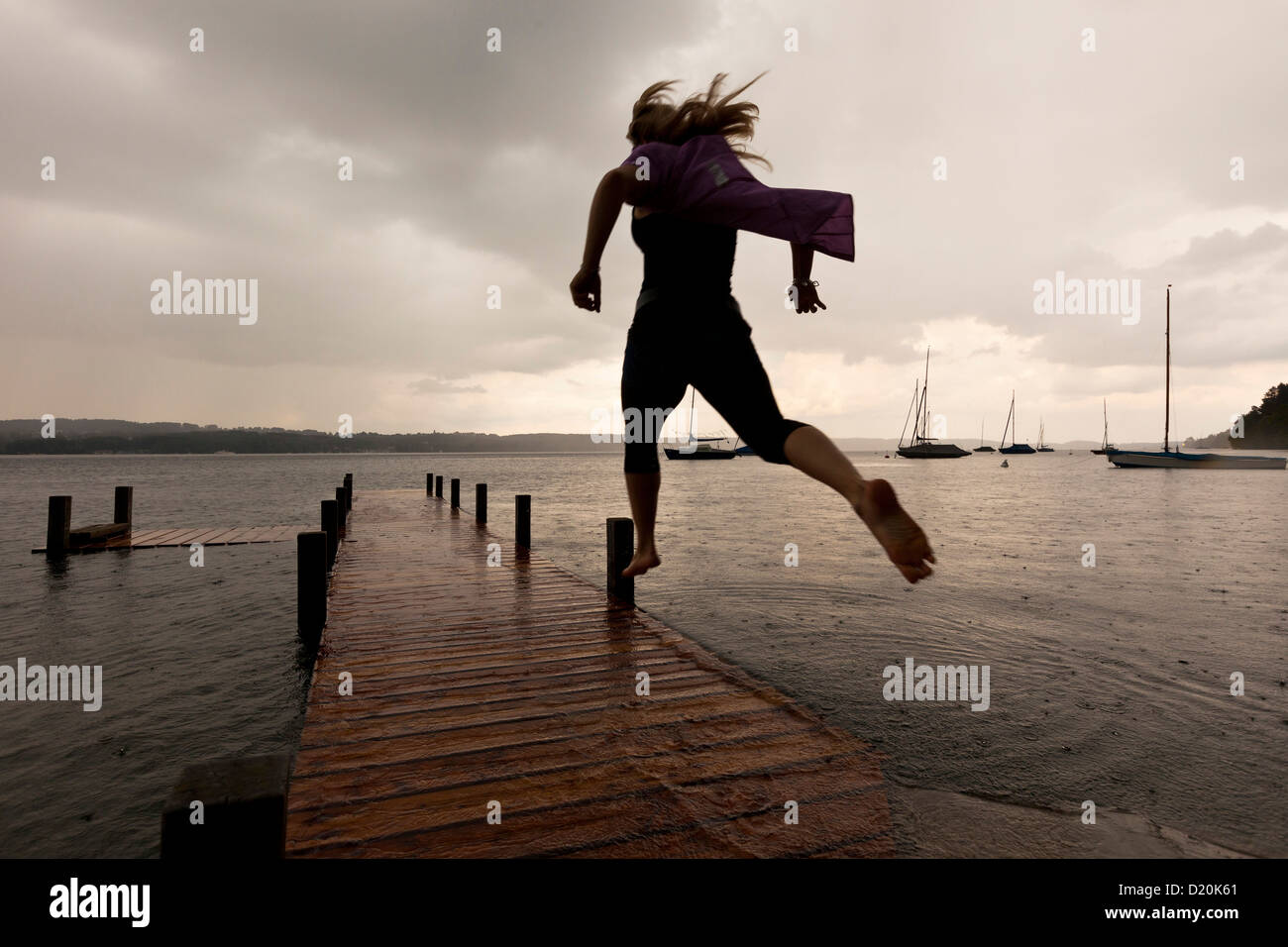 Young woman jumping over pier, high water at Lake Starnberg, Upper ...